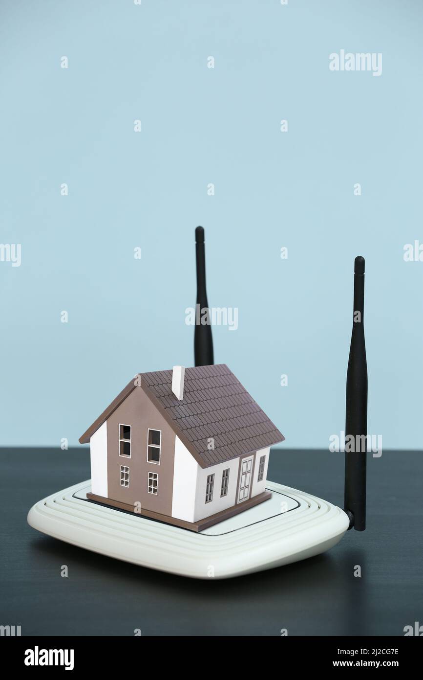 Modern wi-fi router and figure of house on table against light blue ...