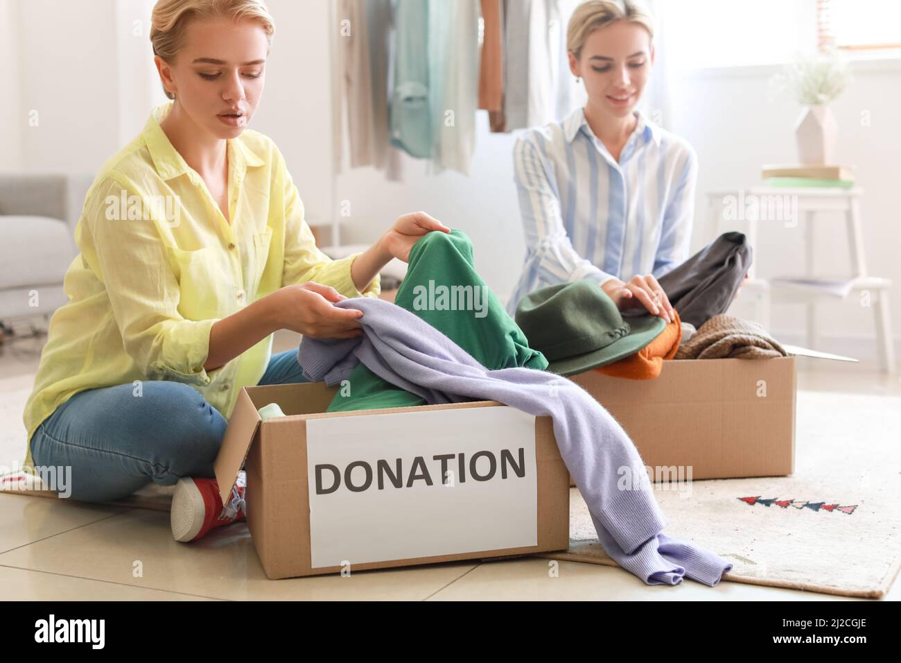 Young women putting clothes in boxes for donation at home Stock Photo ...