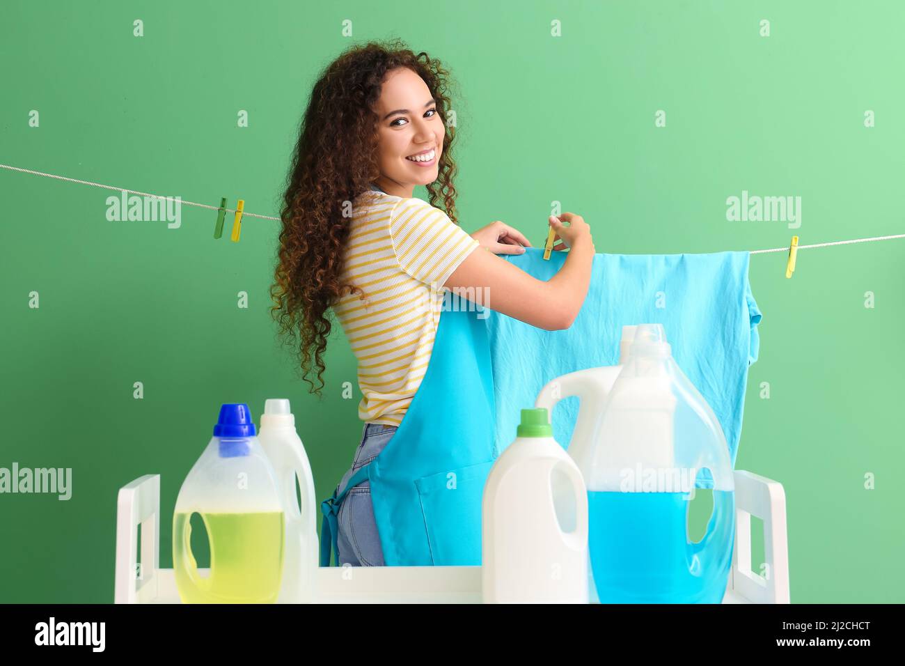 Young African-American woman hanging clean laundry with clothespin on ...