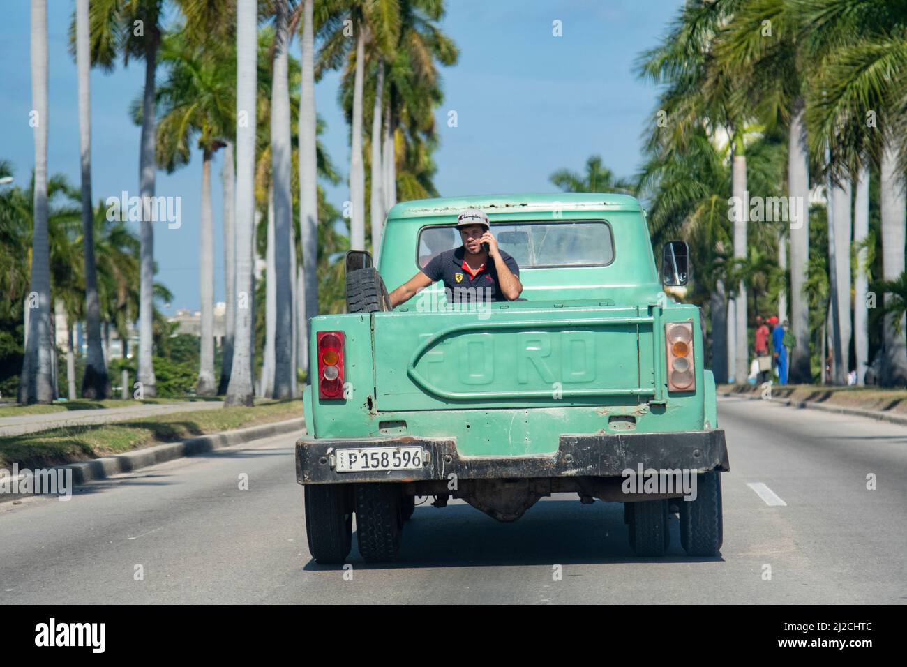 Young Cuban man rides in the back of a pick up truck through a street ...