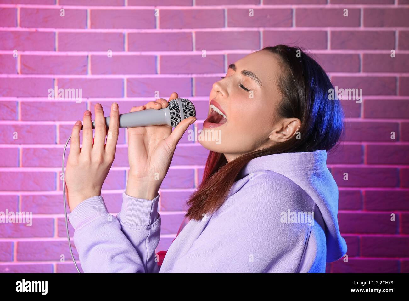 Cool young woman singing on color brick background Stock Photo - Alamy