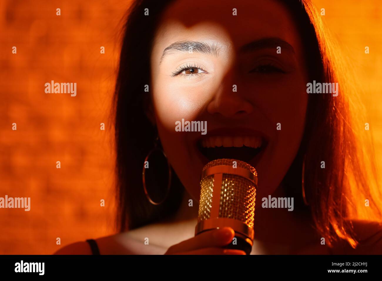 Pretty young singing woman with microphone on color background Stock ...