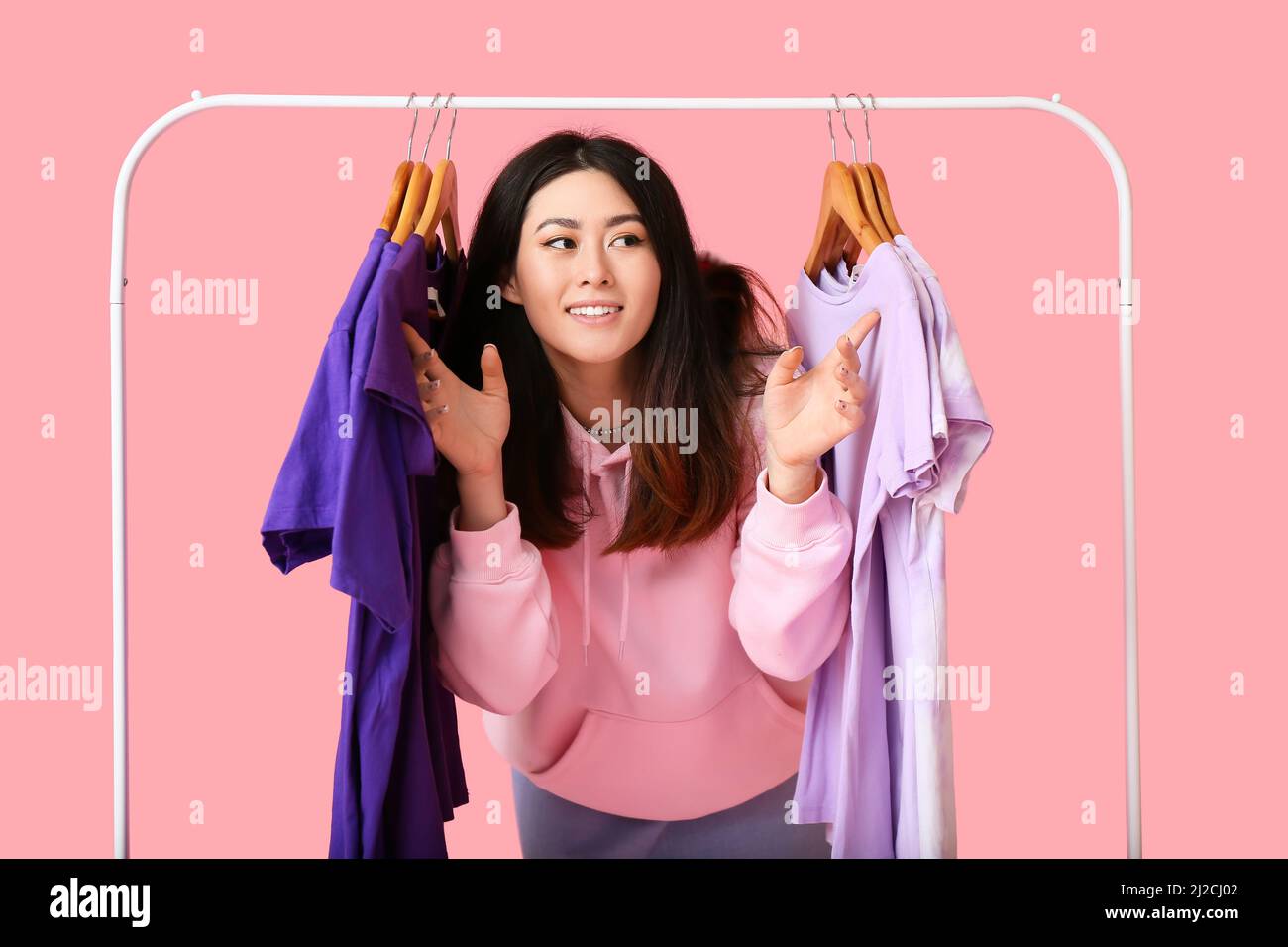 Young Asian woman and rack with t-shirts on pink background Stock Photo ...