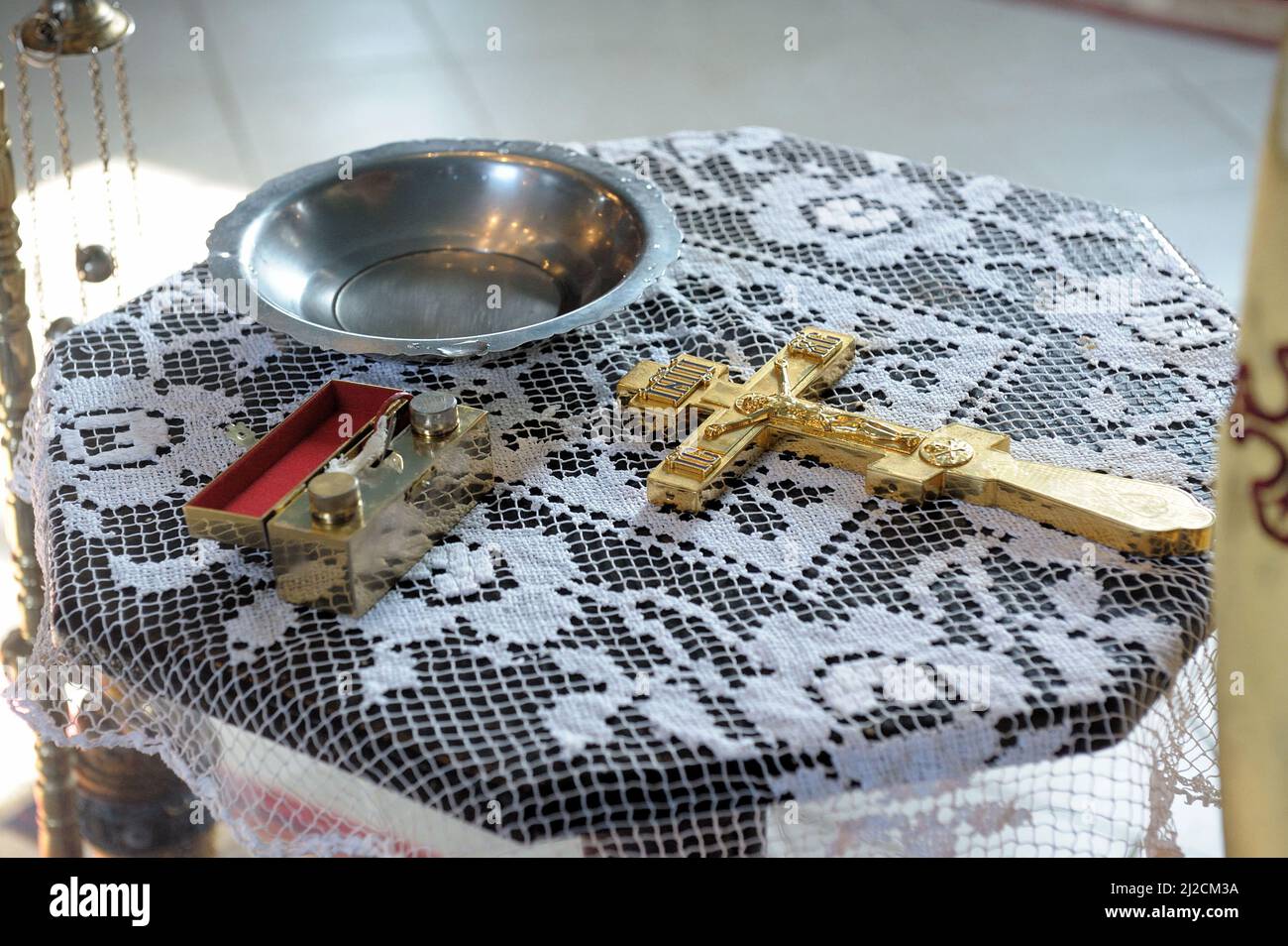 A golden cross and aluminum holy water bowl on a table covered with ...