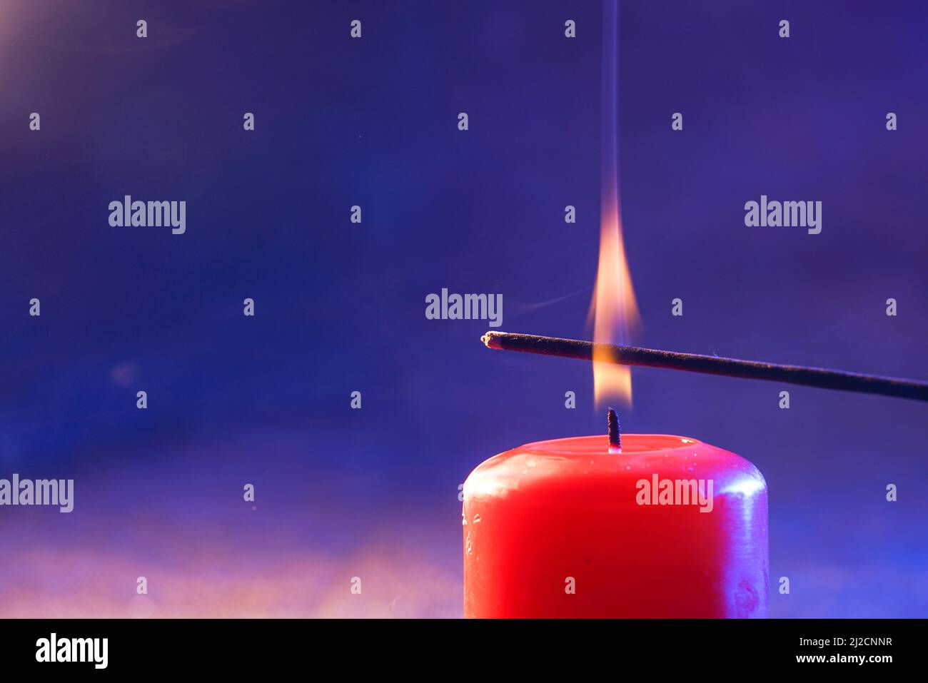 A closeup shot of incense burning on a red candle fire against a purple ...