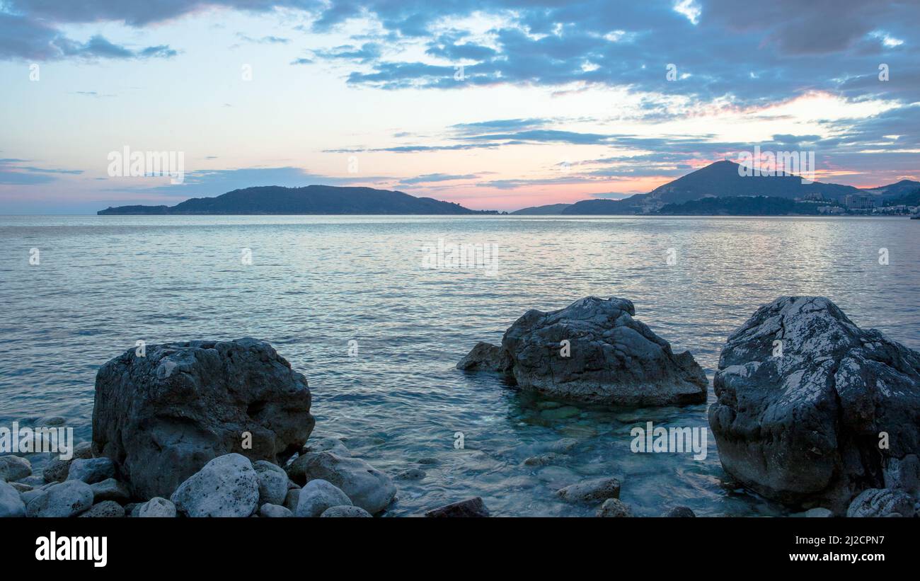 Blue seascape with stoney beach at sunset. Stone coastline with islands ...