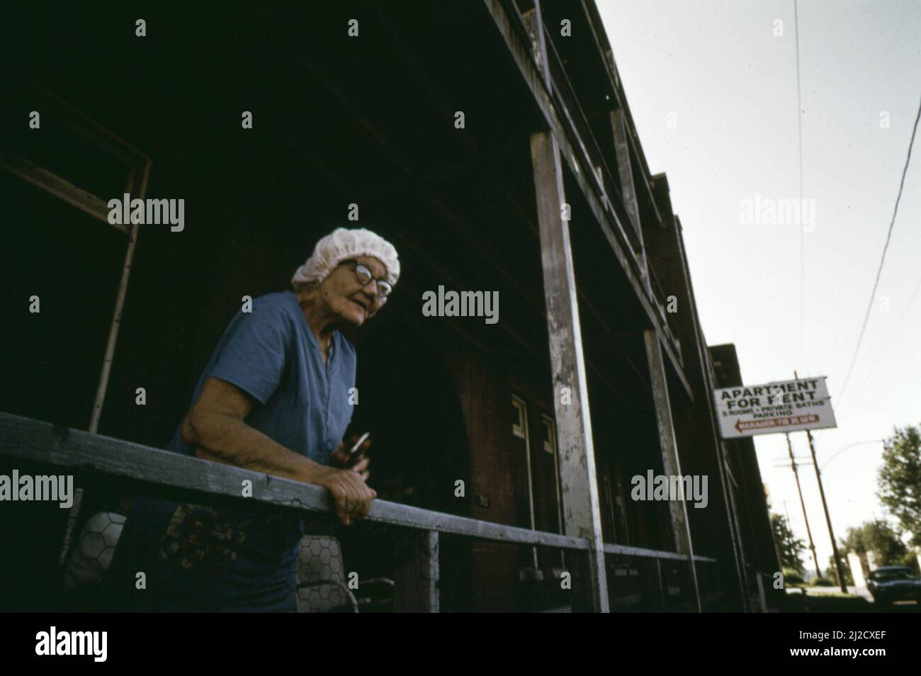 An elderly woman stands on the porch of her apartment homes in the ...