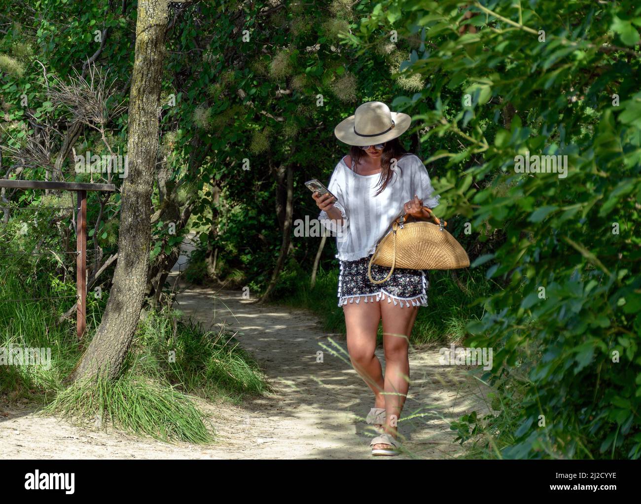A young Caucasian female wearing summer style clothes, walking on path ...