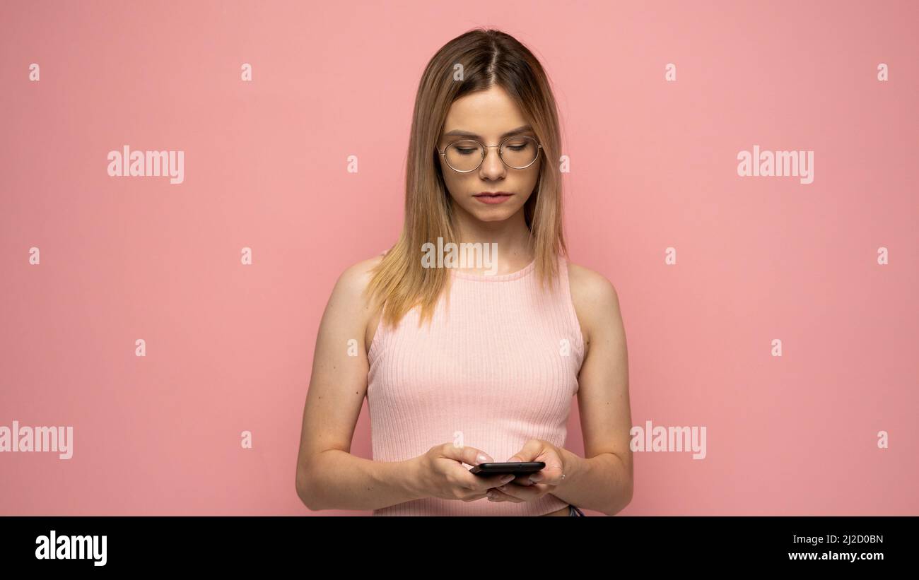 Young happy girl in pink t-shirt using mobile phone, typing sms message ...