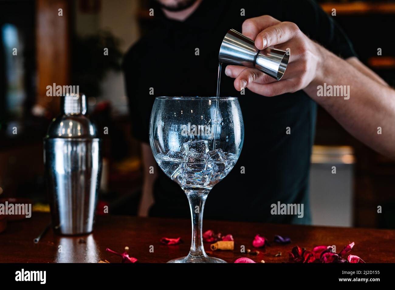 detail of hands bartender pouring liquor into a crystal glass to prepare a mixed drink at the ...