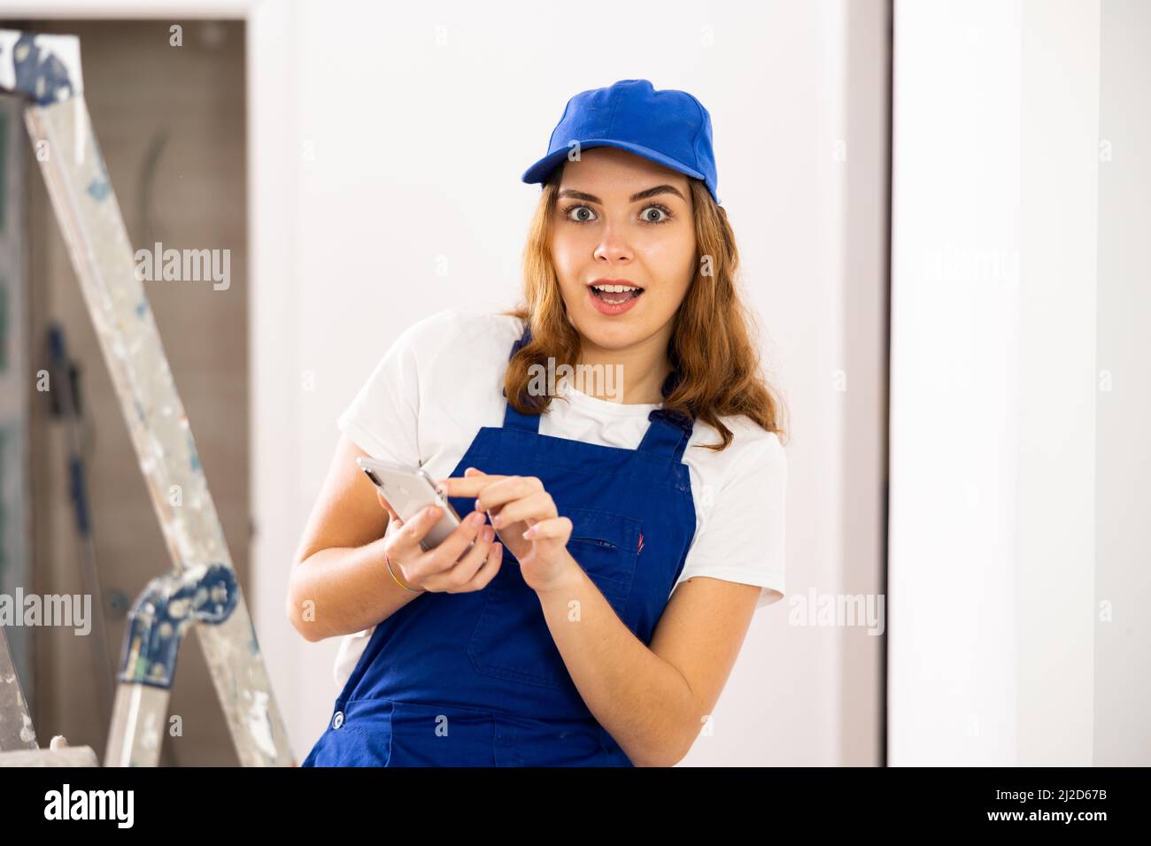 Happy surprised female builder reading message on smartphone Stock ...