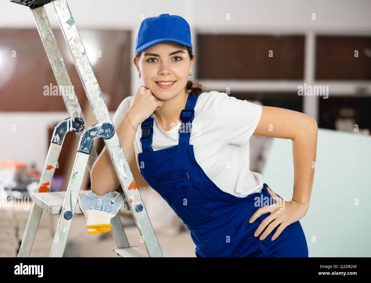 Positive builder woman in blue overalls next to stepladder Stock Photo ...