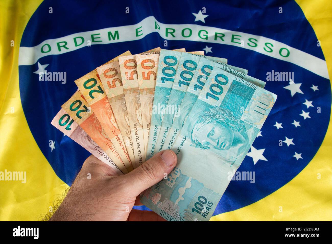 Hand holding Brazilian money banknotes with Brazilian flag in the ...