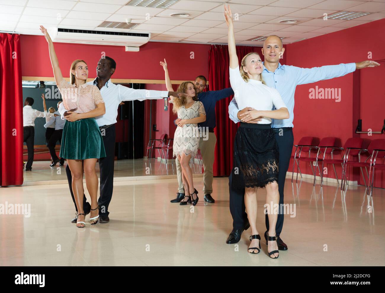 Portrait of positive adult pairs enjoying tango in modern dance hall ...