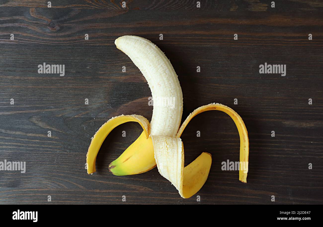 A finger of peeled fresh ripe banana isolated on black wooden backdrop ...