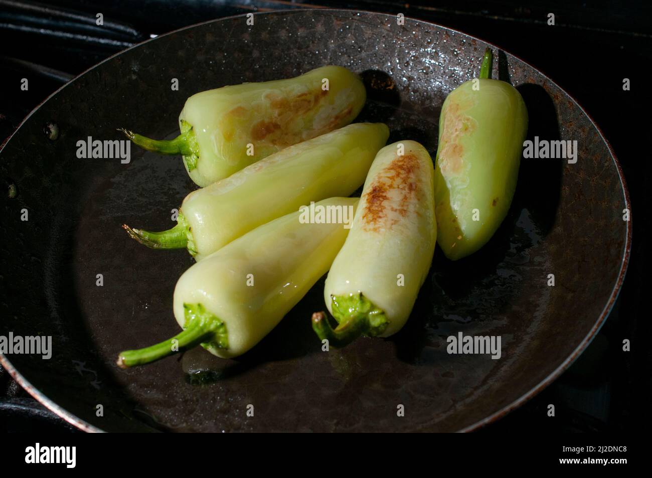 Frying a group of yellow hot peppers on a pan with oil macro ...