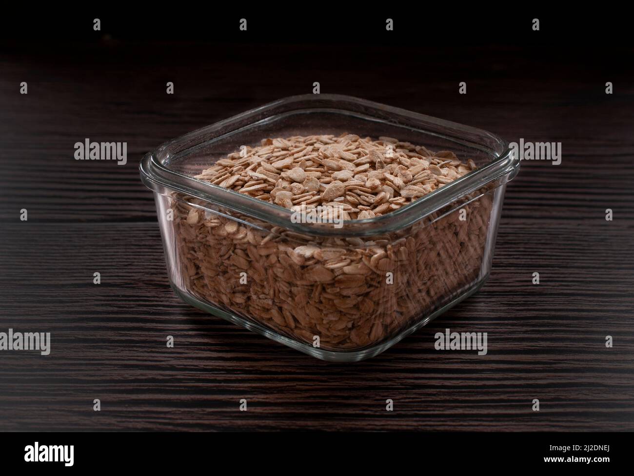 Raw oatmeal in a square glass container over a dark wooden table, dark ...