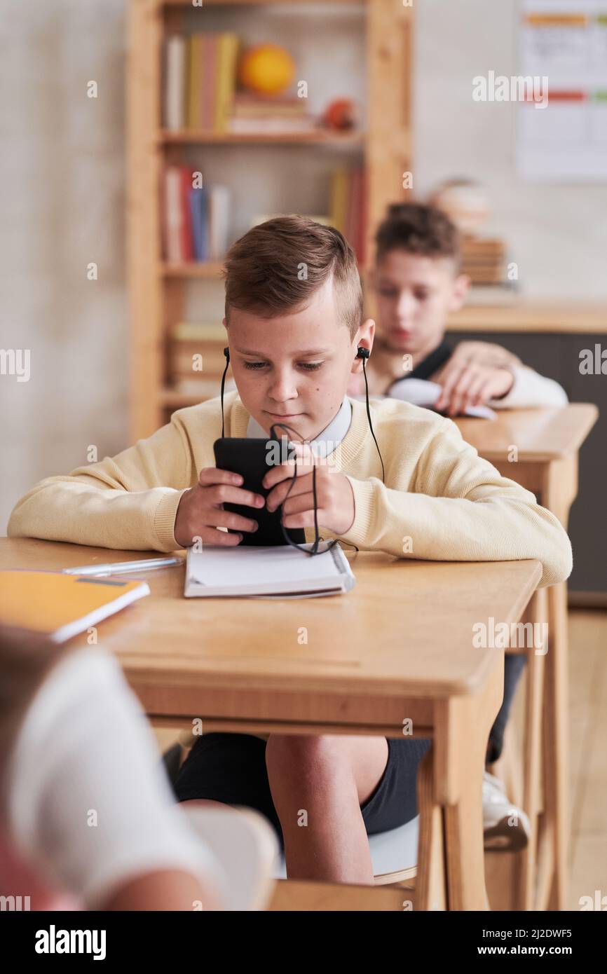 Vertical portrait of young boy using smartphone in school while sitting ...