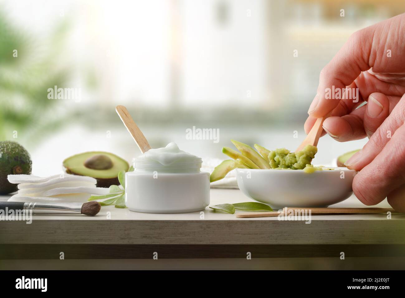 Hands preparing natural avocado skin care cream made in home kitchen ...