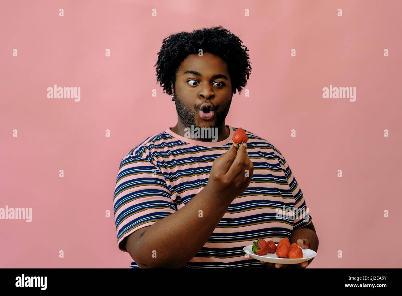 young happy african american man eating strawberries in the studio over ...