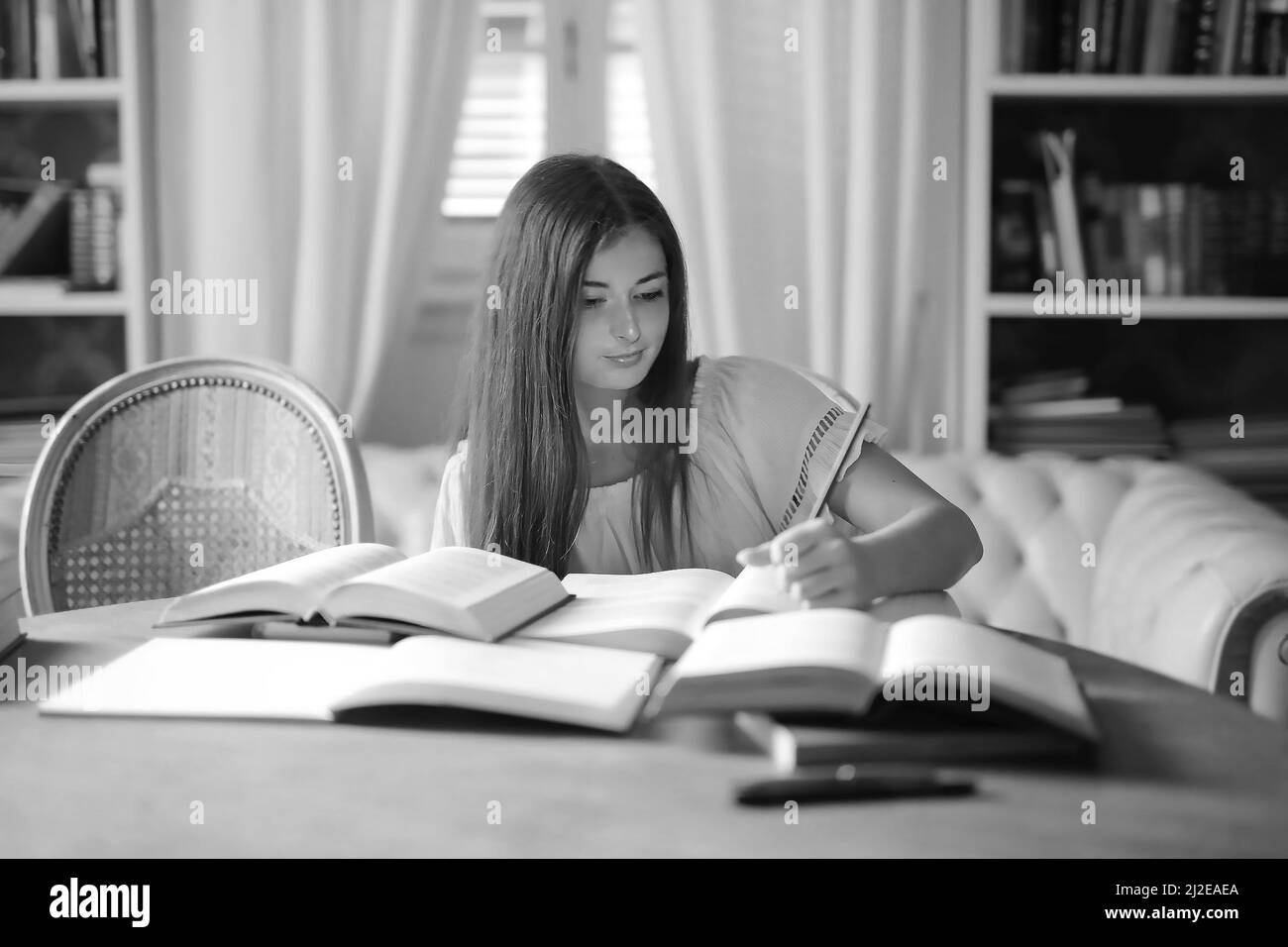 Pretty young teenage girl doing her homework, surrounded by open books ...