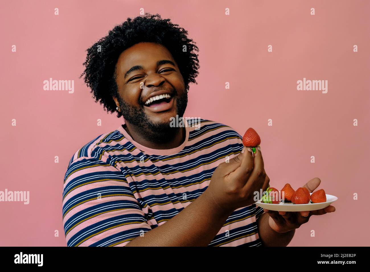 young happy african american man eating strawberries in the studio over ...