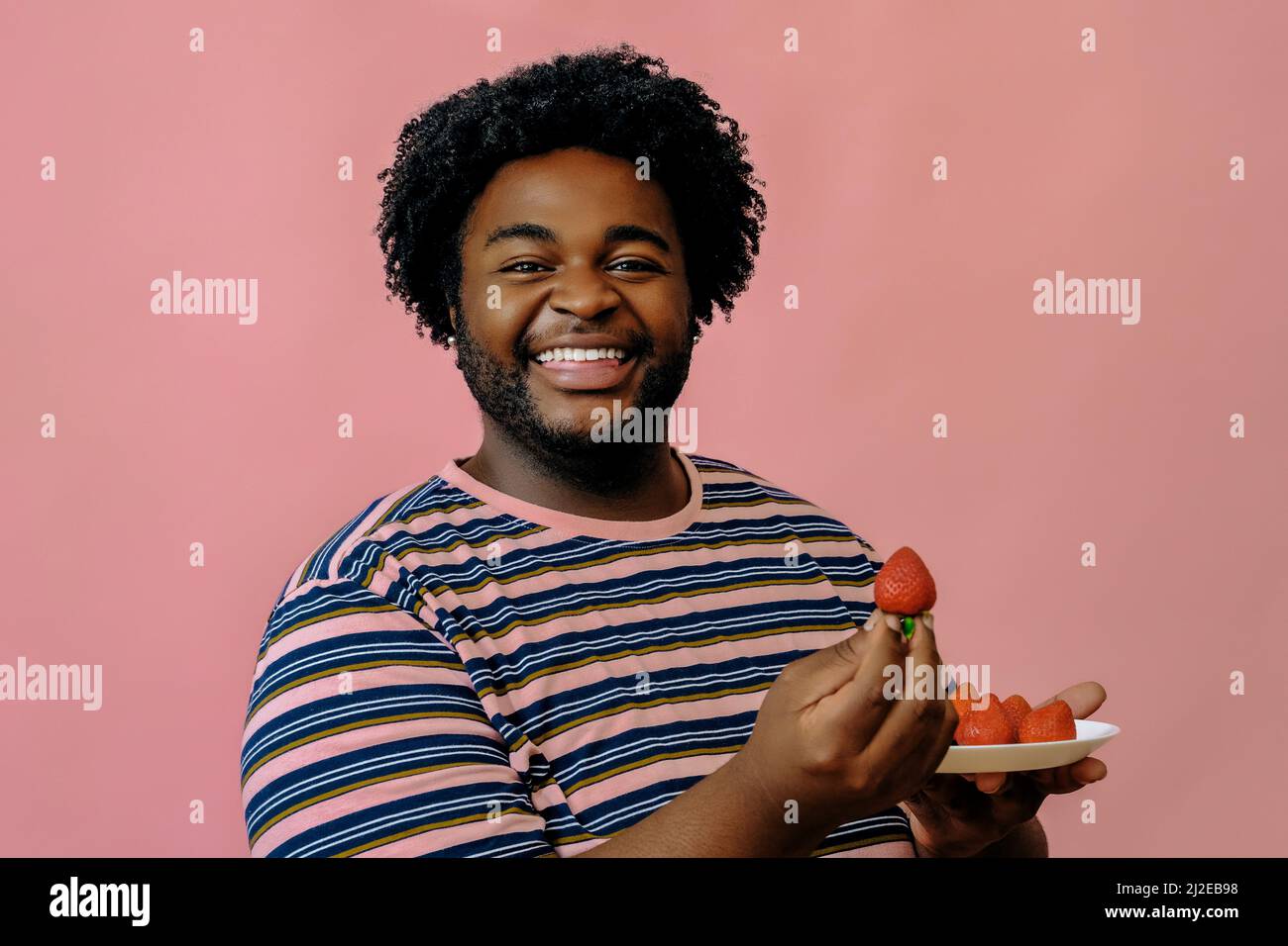 young happy african american man eating strawberries in the studio over ...