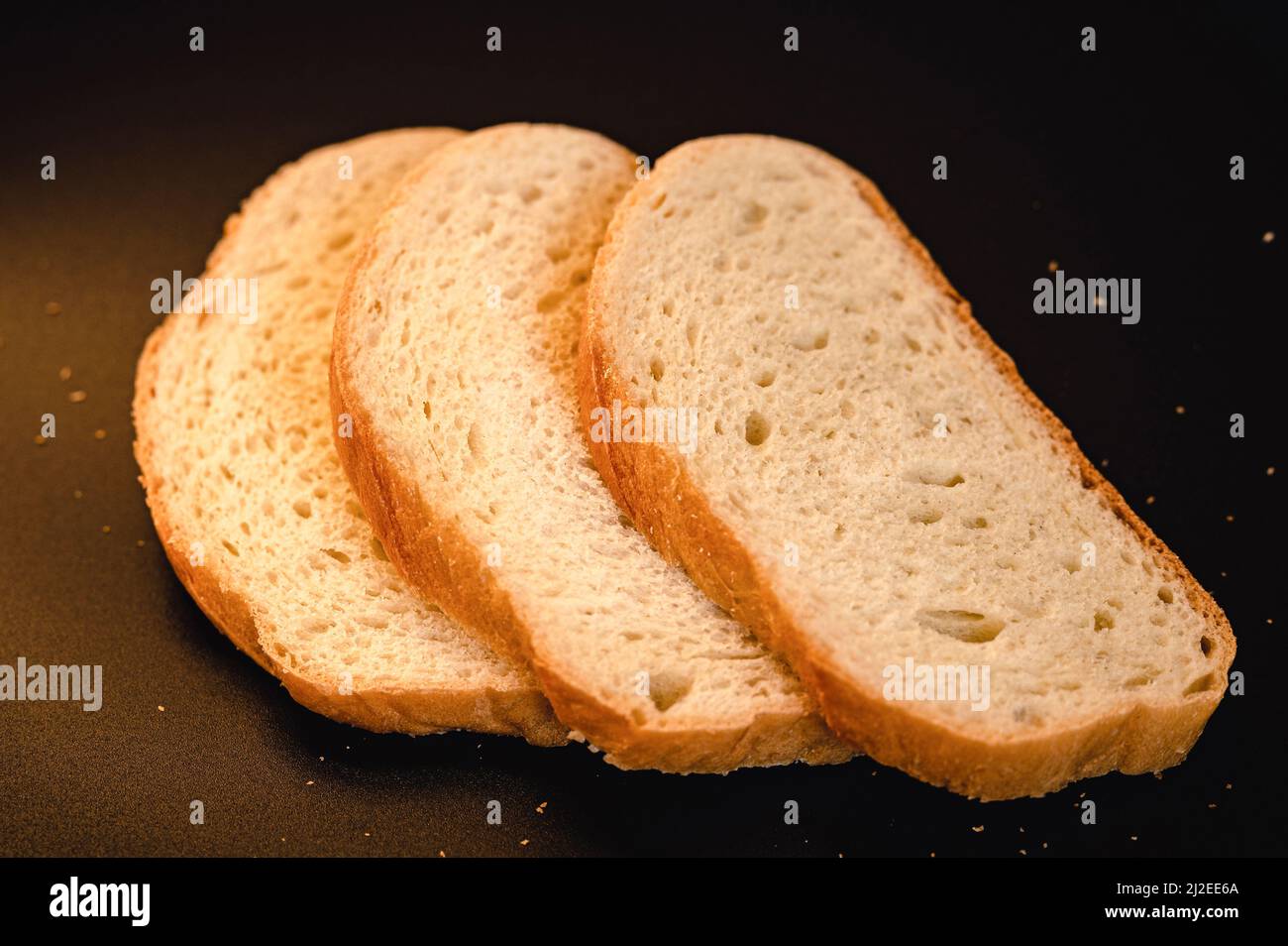 slices of white bread close up on a black background. rough dappled ...