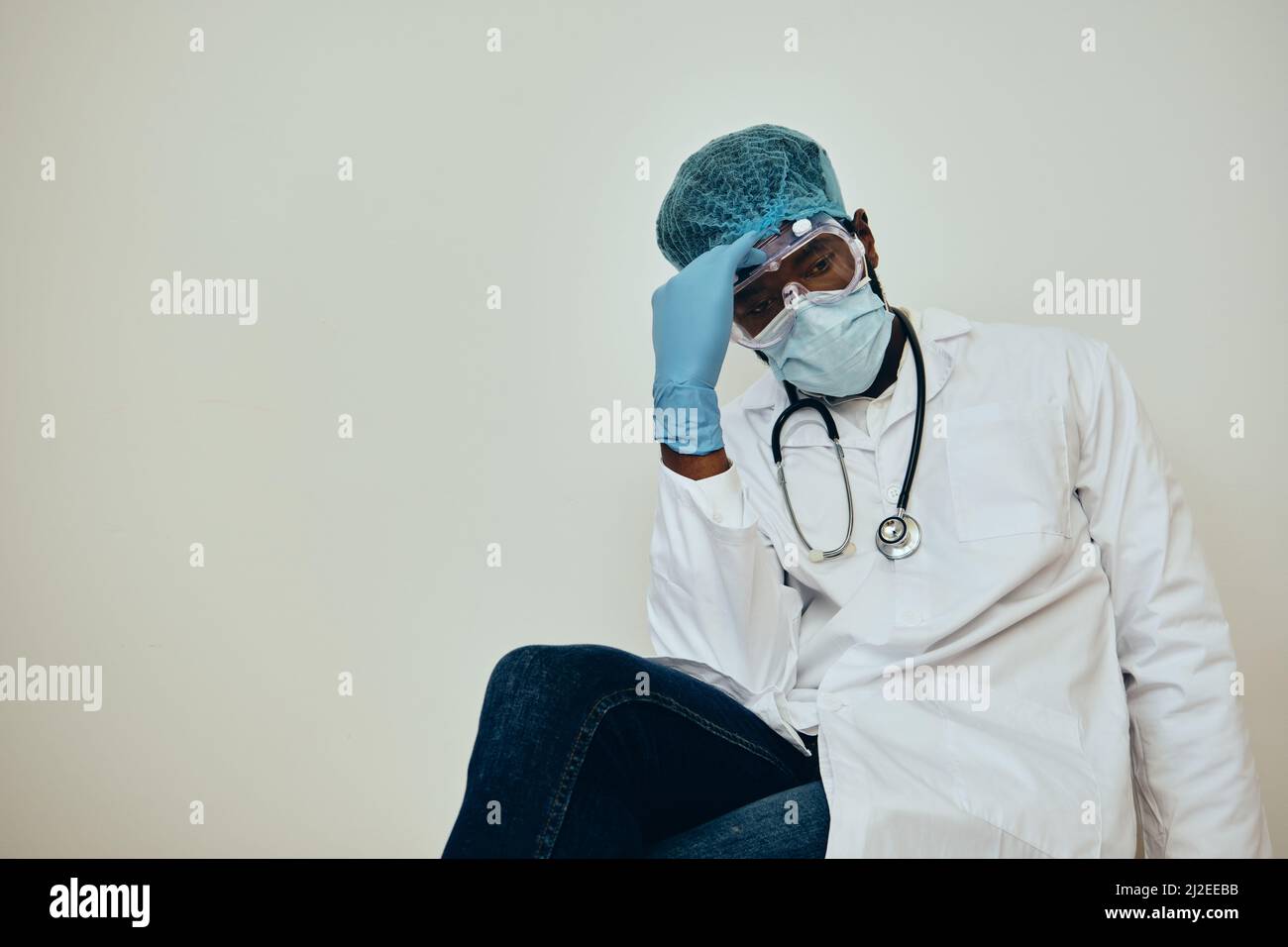 Exhausted male healthcare worker sitting on chair against white wall at ...