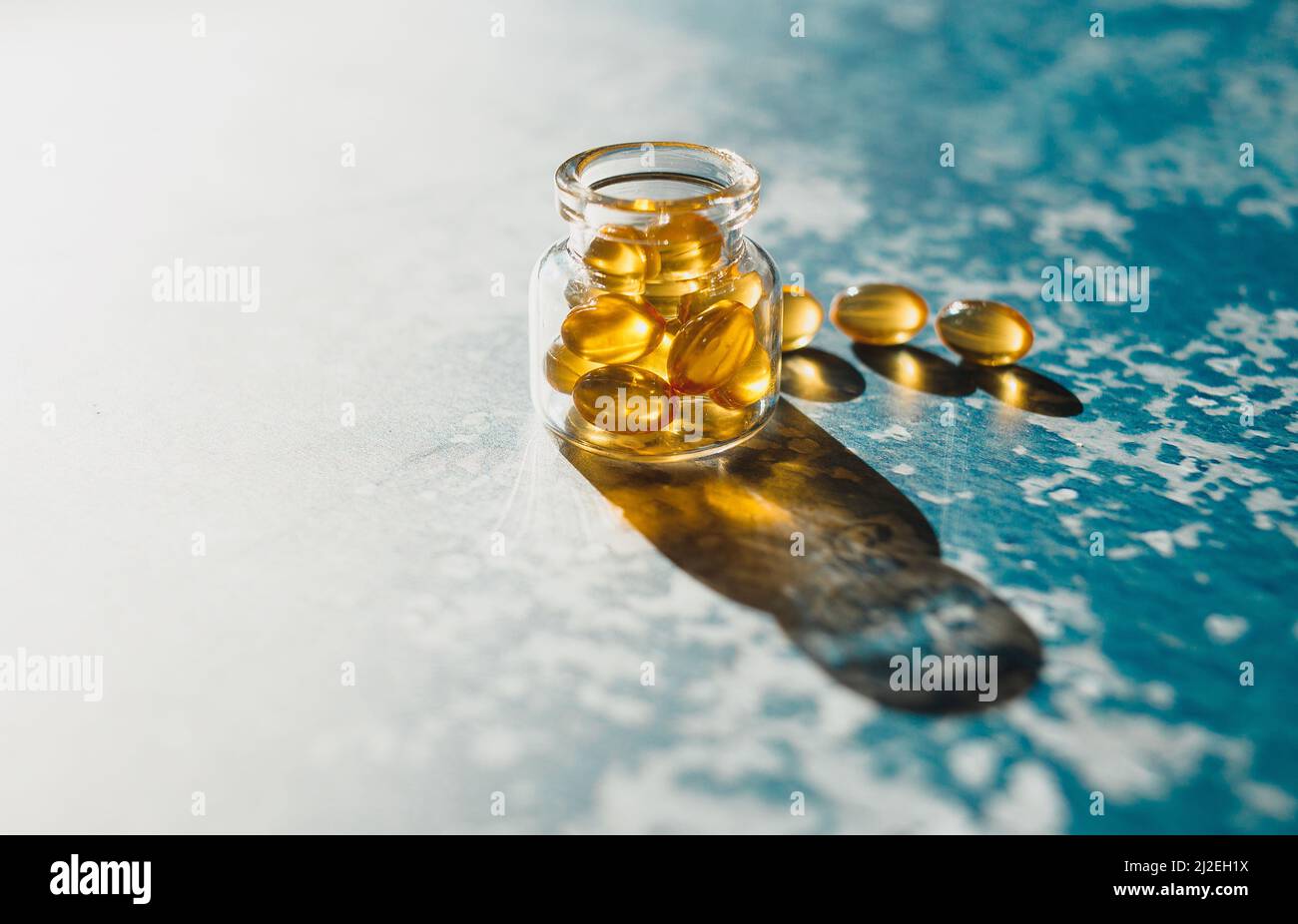 Yellow cod liver capsules lined in a glass bottle on a blue background ...
