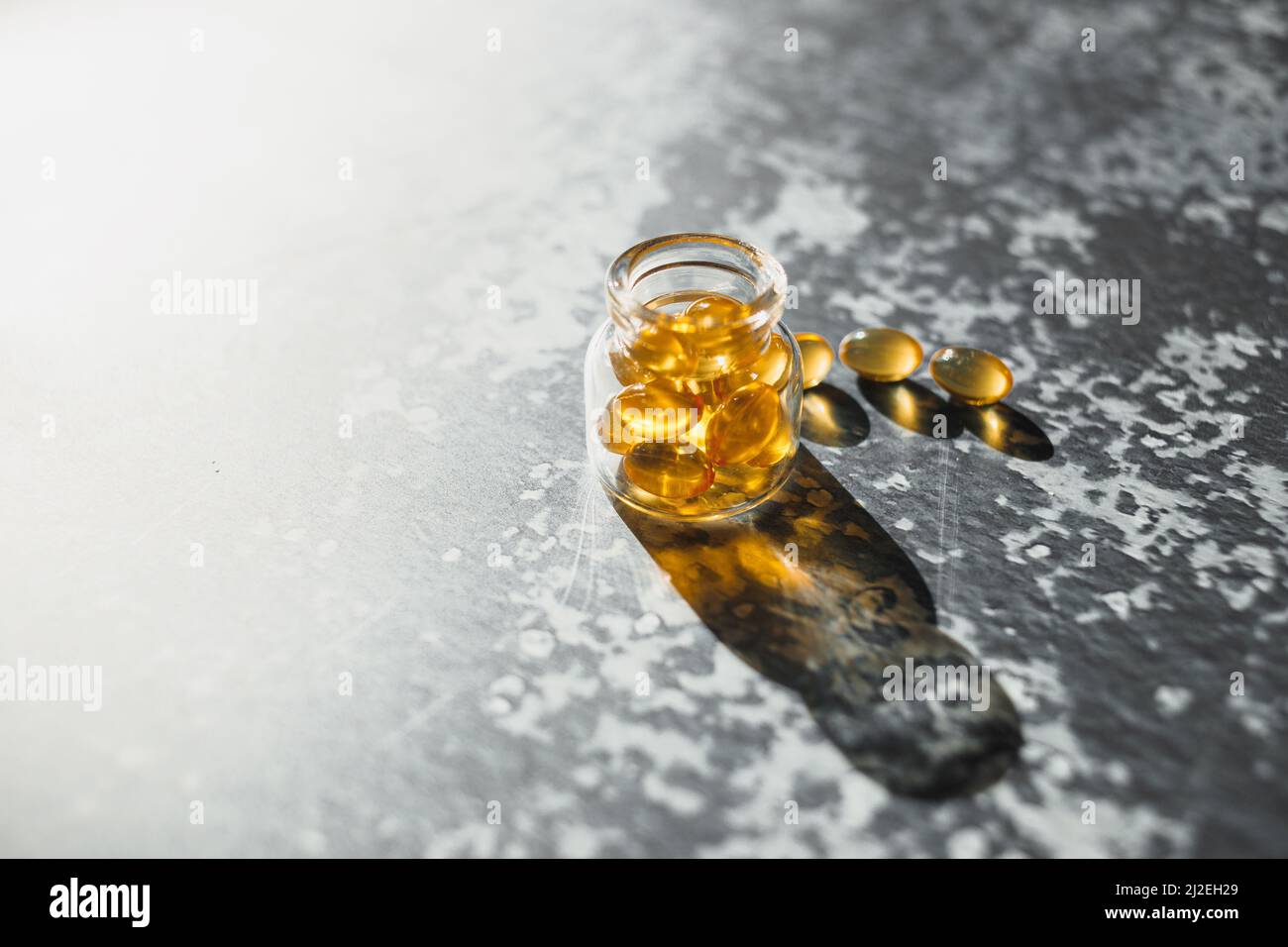 Yellow cod liver capsules lined in a glass bottle on a gray background ...