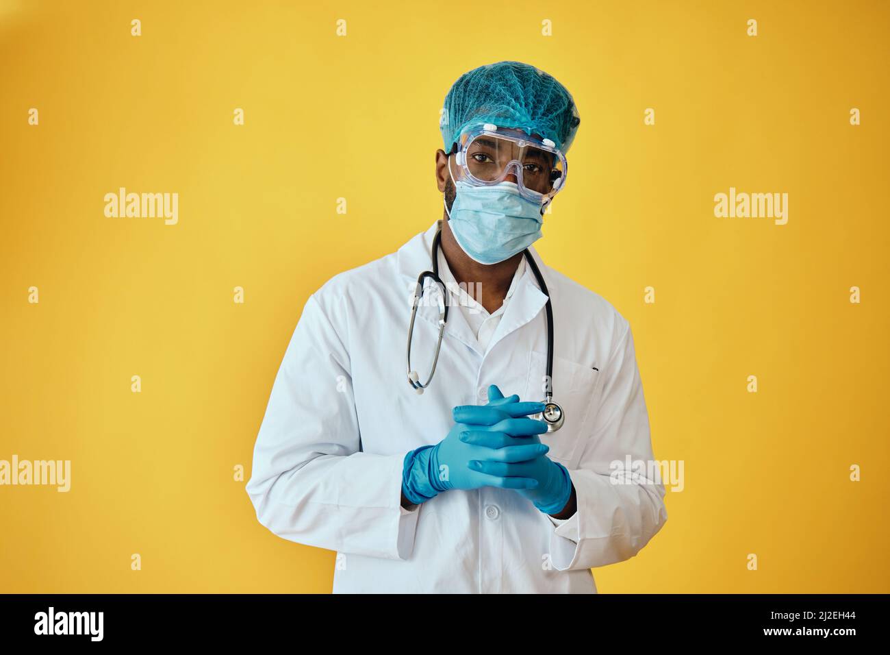 Portrait of male doctor wearing protection from COVID-19 against yellow ...