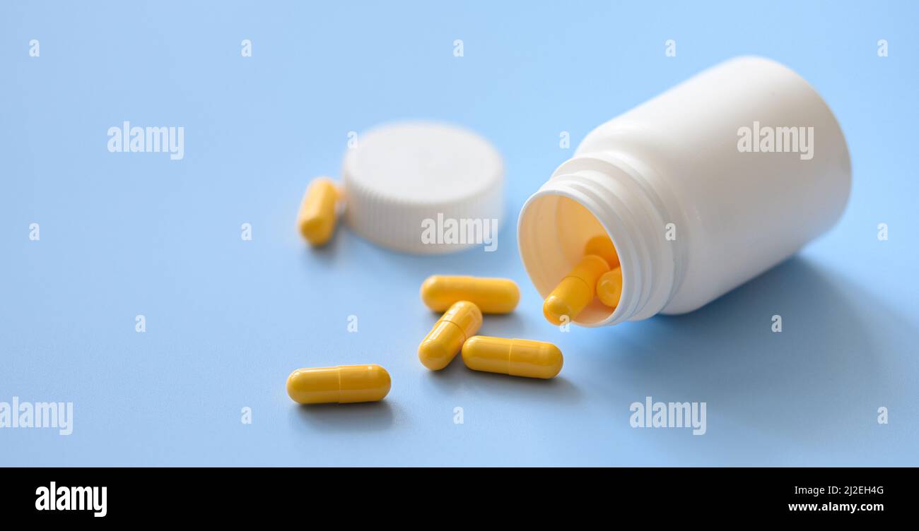 Yellow capsules scattered from white plastic medicine container Stock ...