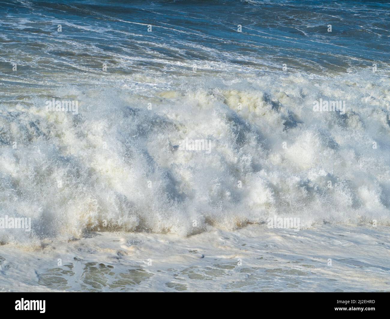 White foamy water churning as wild waves break near shore, crashing and ...