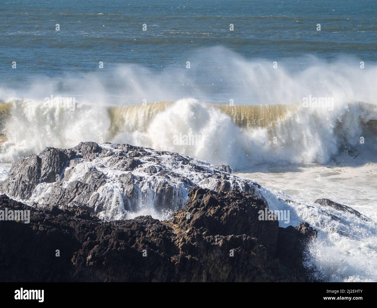 Ocean waves rolling in and crashing over rocks, dirty and frothy after ...