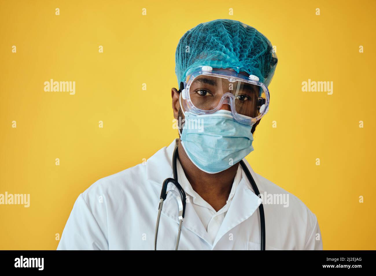 Portrait of male doctor wearing protection from COVID-19 against yellow ...