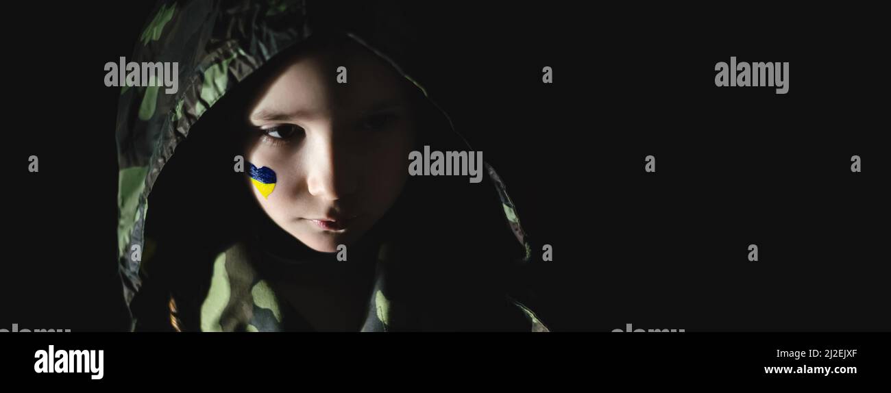 sad kid with painted ukrainian flag on cheek isolated on black, banner ...