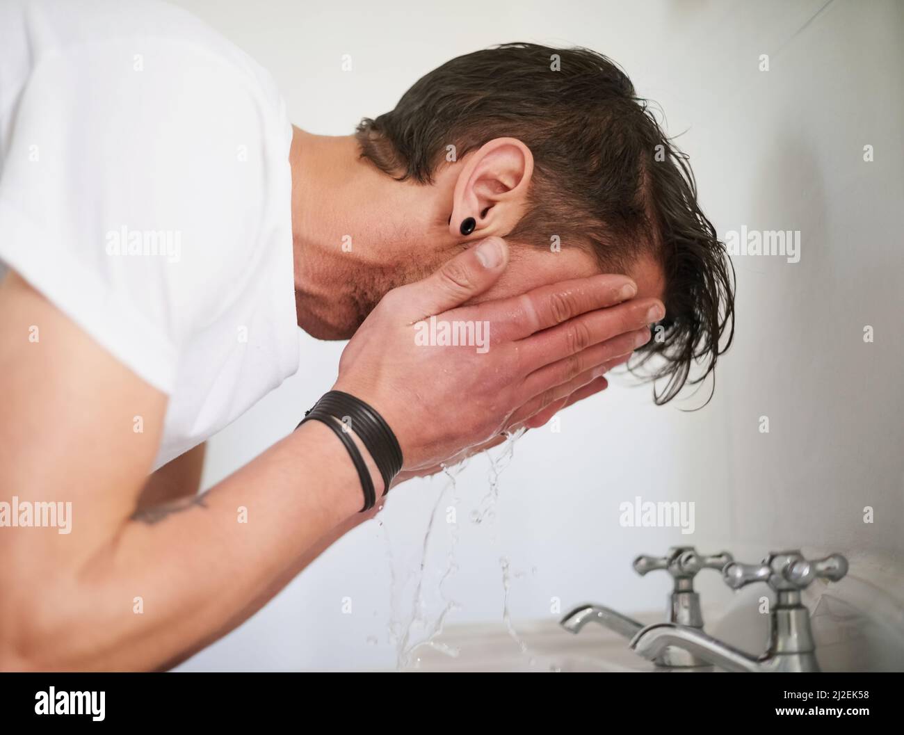 Freshening up in the morning. Shot of a young man washing his face in a bathroom sink Stock ...
