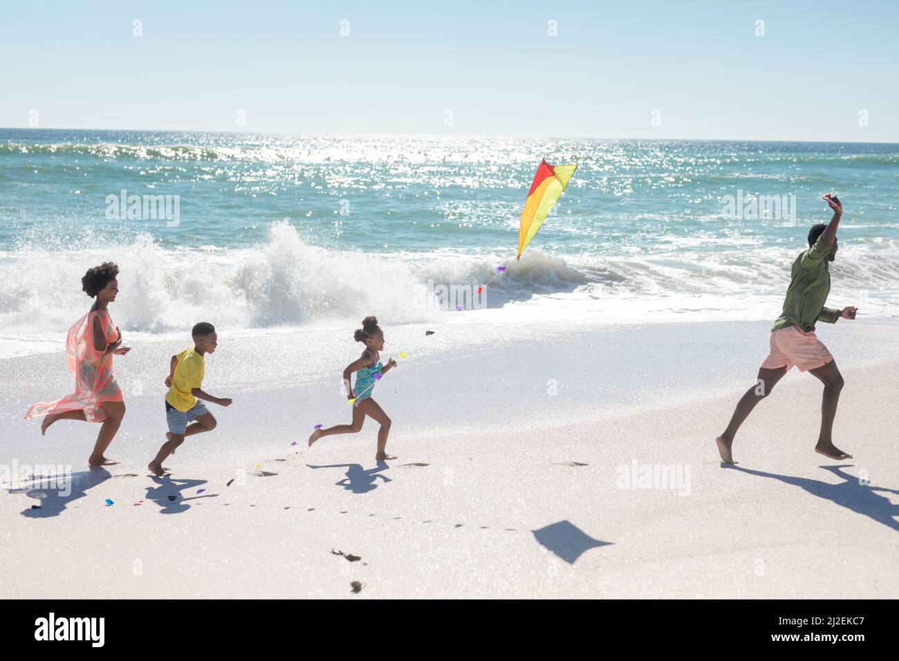 African american father running with kite ahead of family on shore at ...