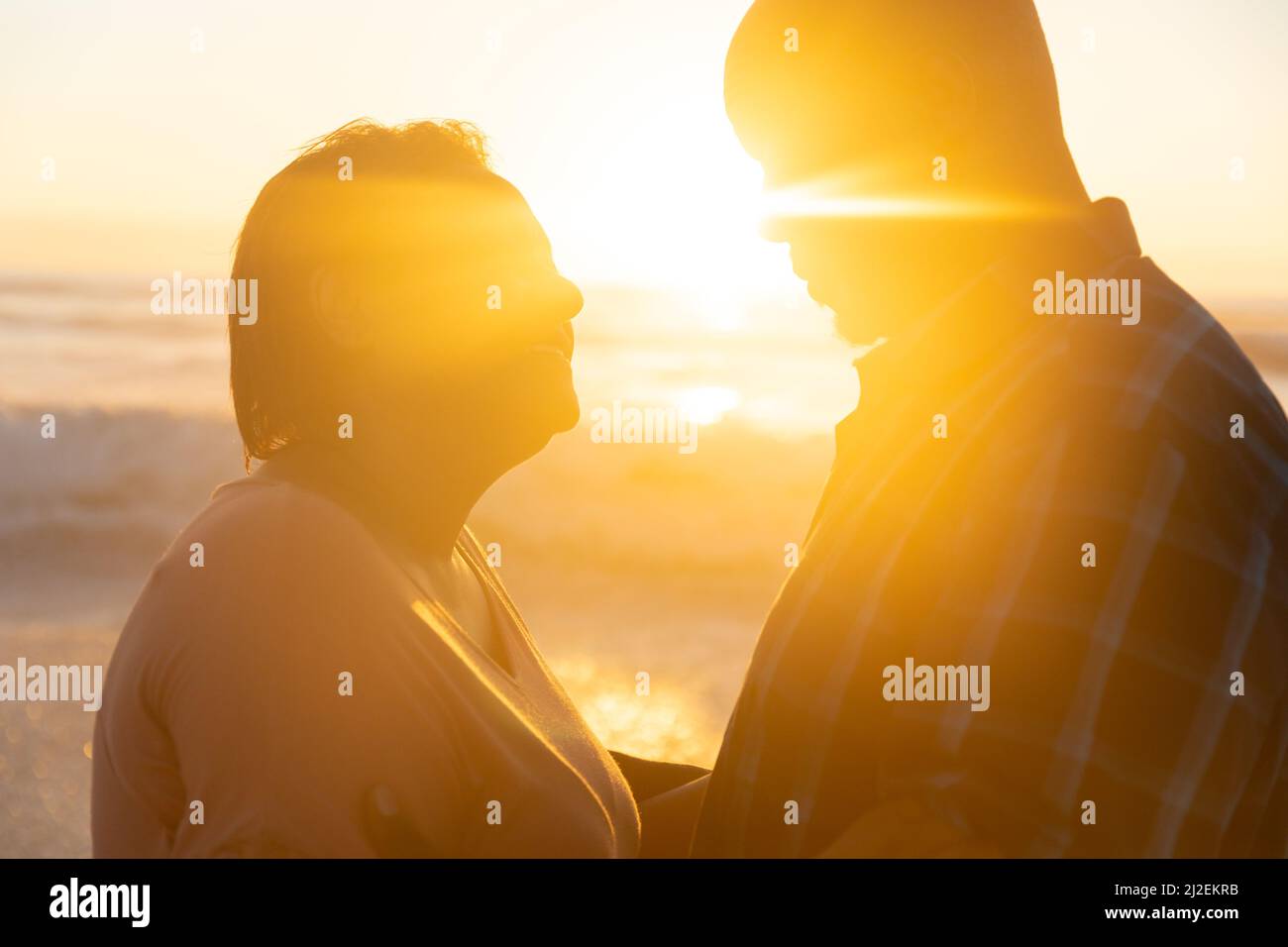 Back lit african american senior couple standing face to face at beach ...