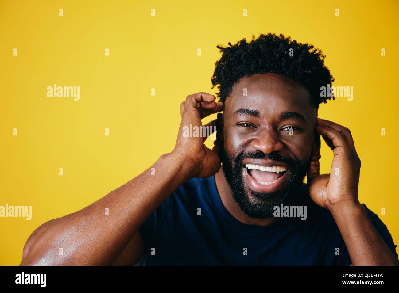 Portrait of playful Afro man with mouth open touching ears against ...