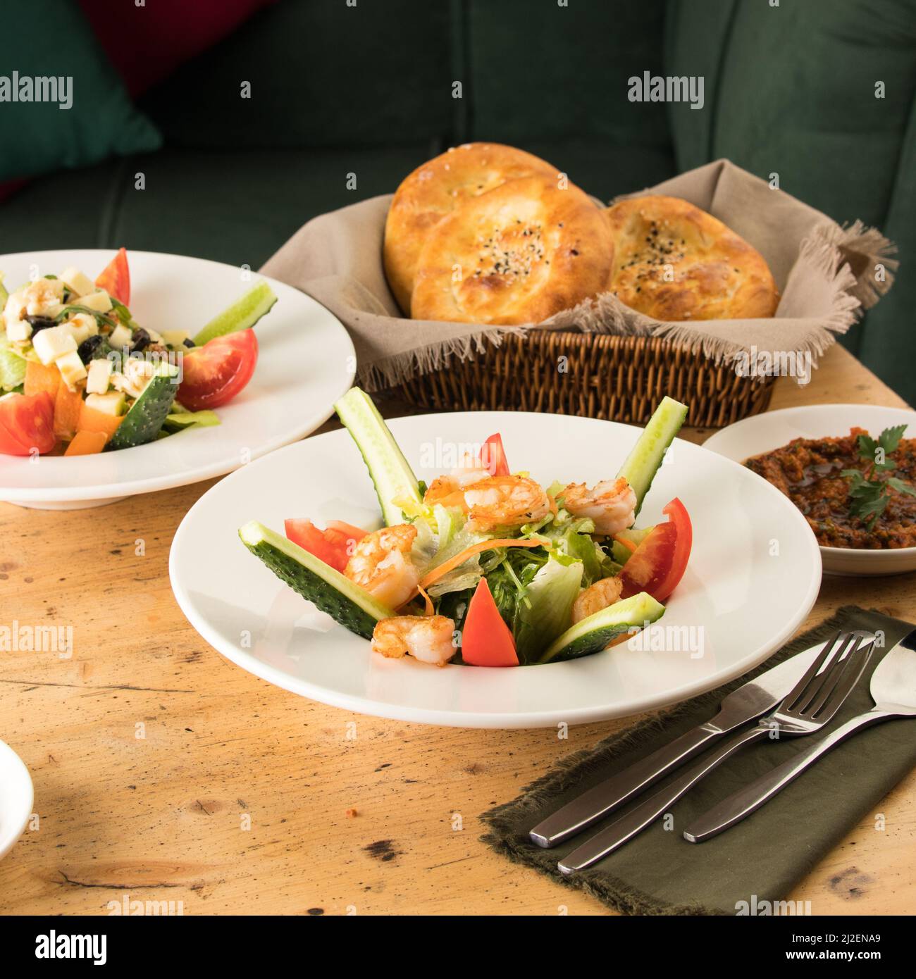 A dining table full of delicious salads on white plates next to basket ...