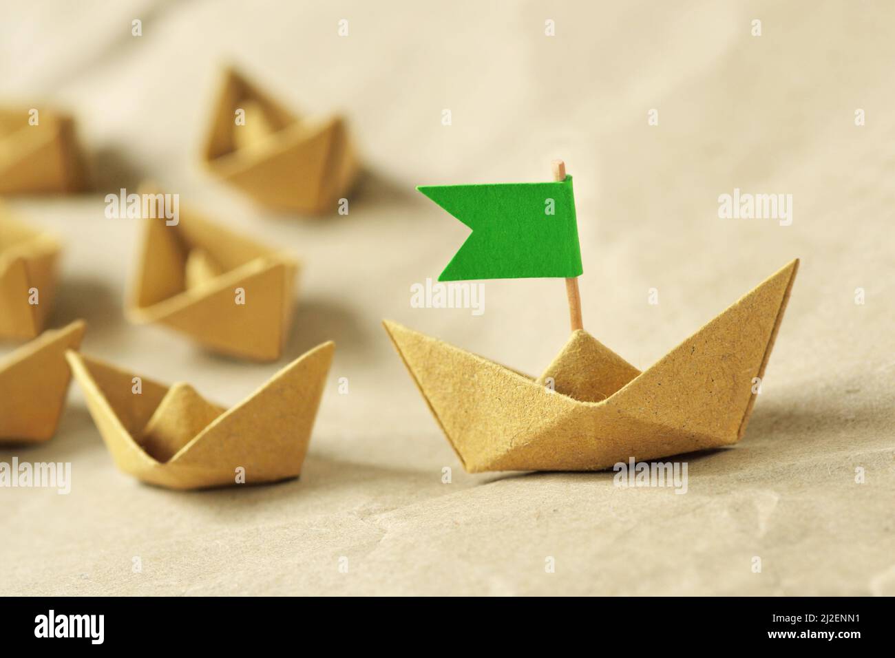 Origami recycled paper boat with green flag leading a group of small ...
