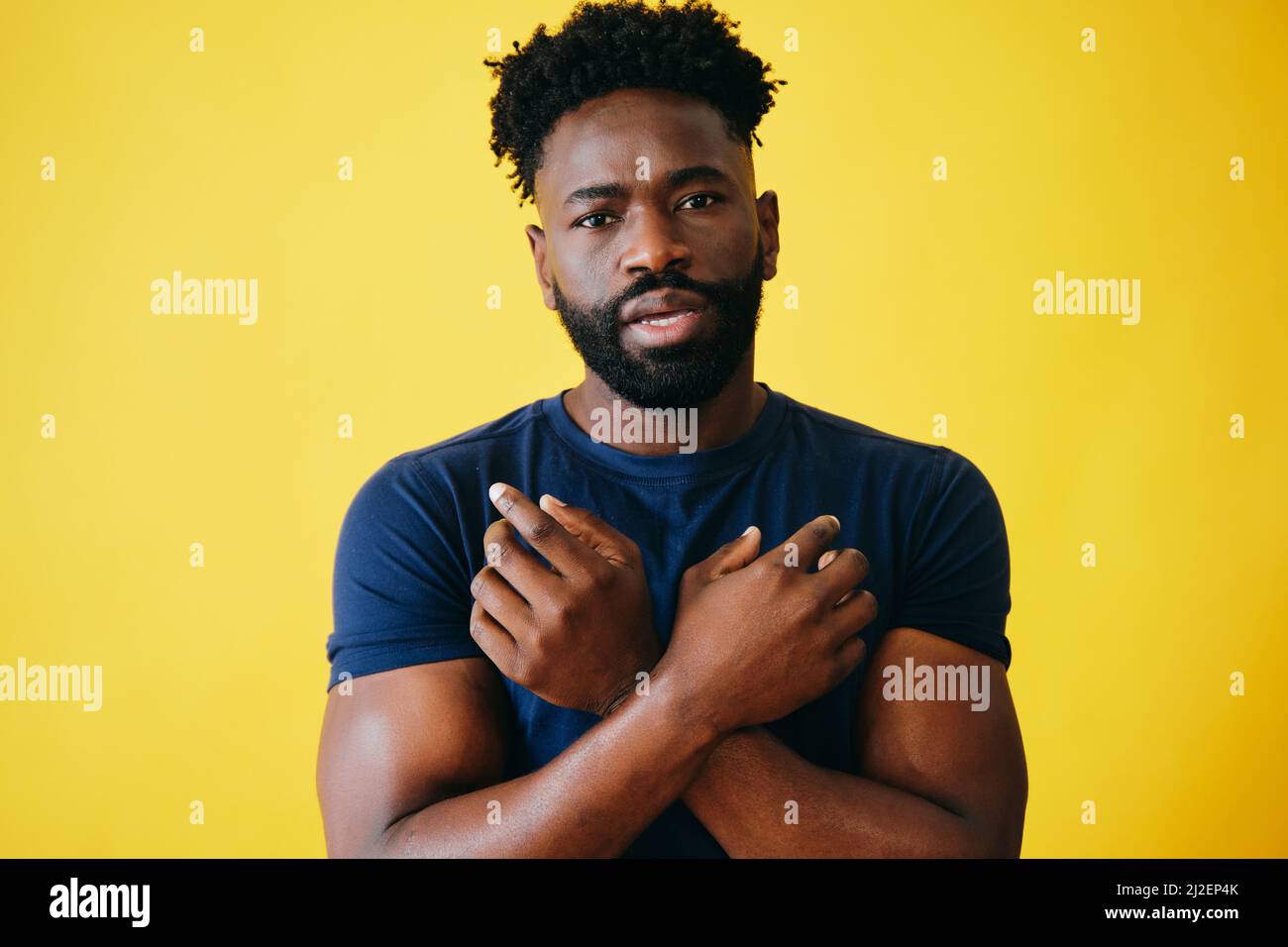 Confident muscular Afro man with hands crossed against yellow ...