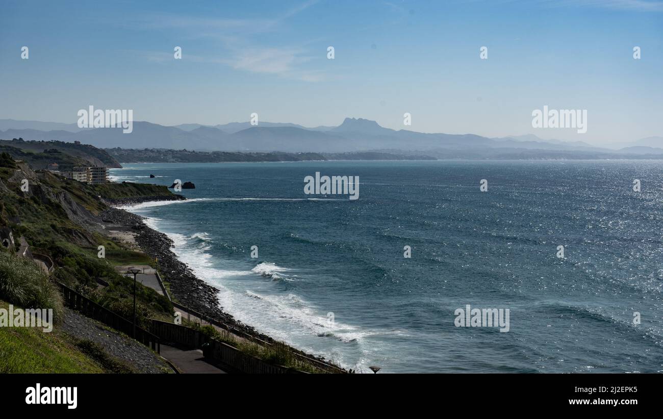 A body of water with the waves hitting the shore under a light blue sky ...
