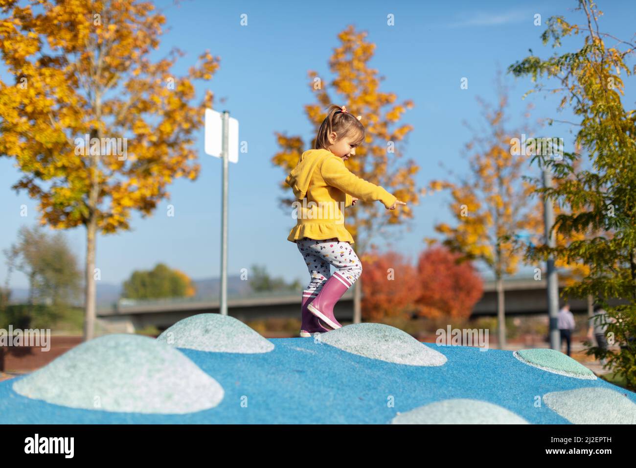 2-years old girl running rubber hills at playground on sunny autumn day ...