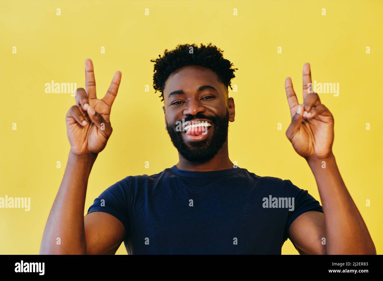 Portrait of playful Afro man sticking out tongue while showing peace ...