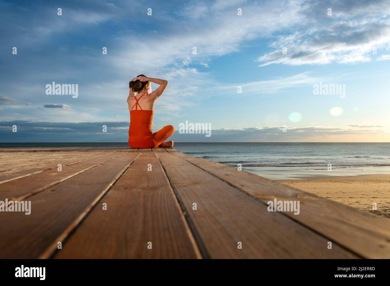 sporty woman sitting, tying her hair up and relaxing watching the sun ...