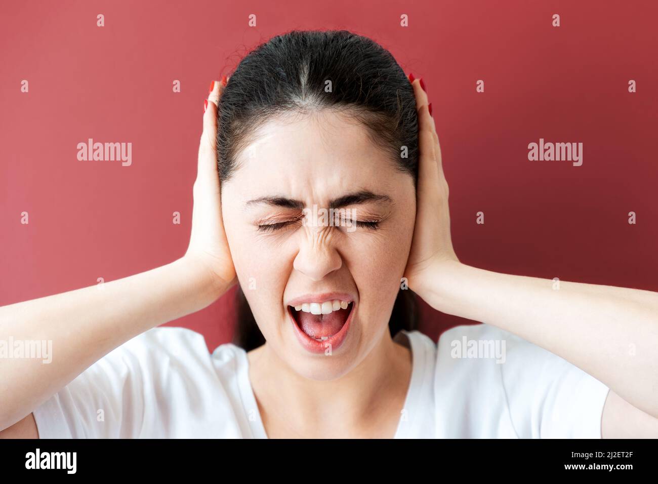 Portrait of a screaming young Caucasian woman covering her ears with ...