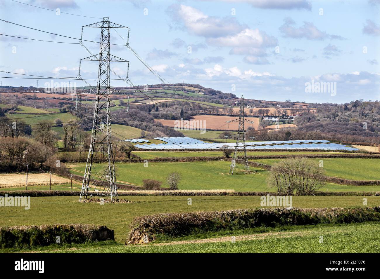 A solar farm and electric pylons pictured in the green fields of ...